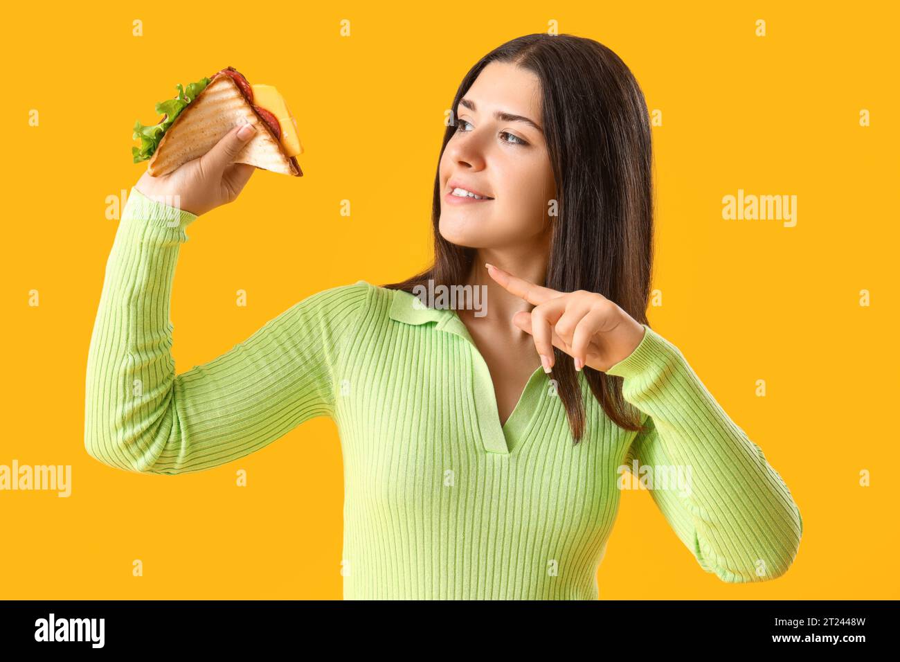 Young woman pointing at tasty sandwich on yellow background Stock Photo ...