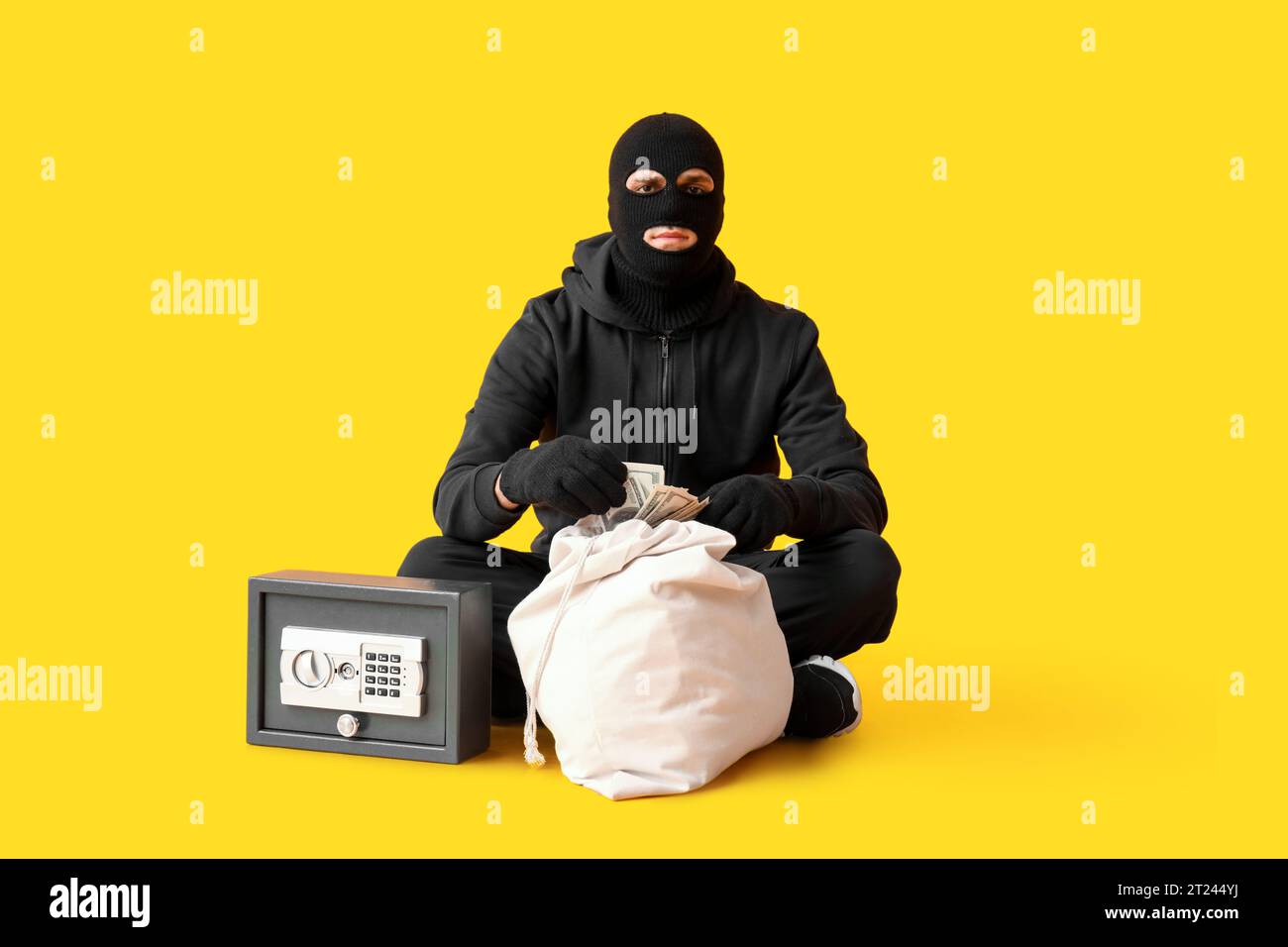 Male thief with safe box and bag of money sitting on yellow background ...