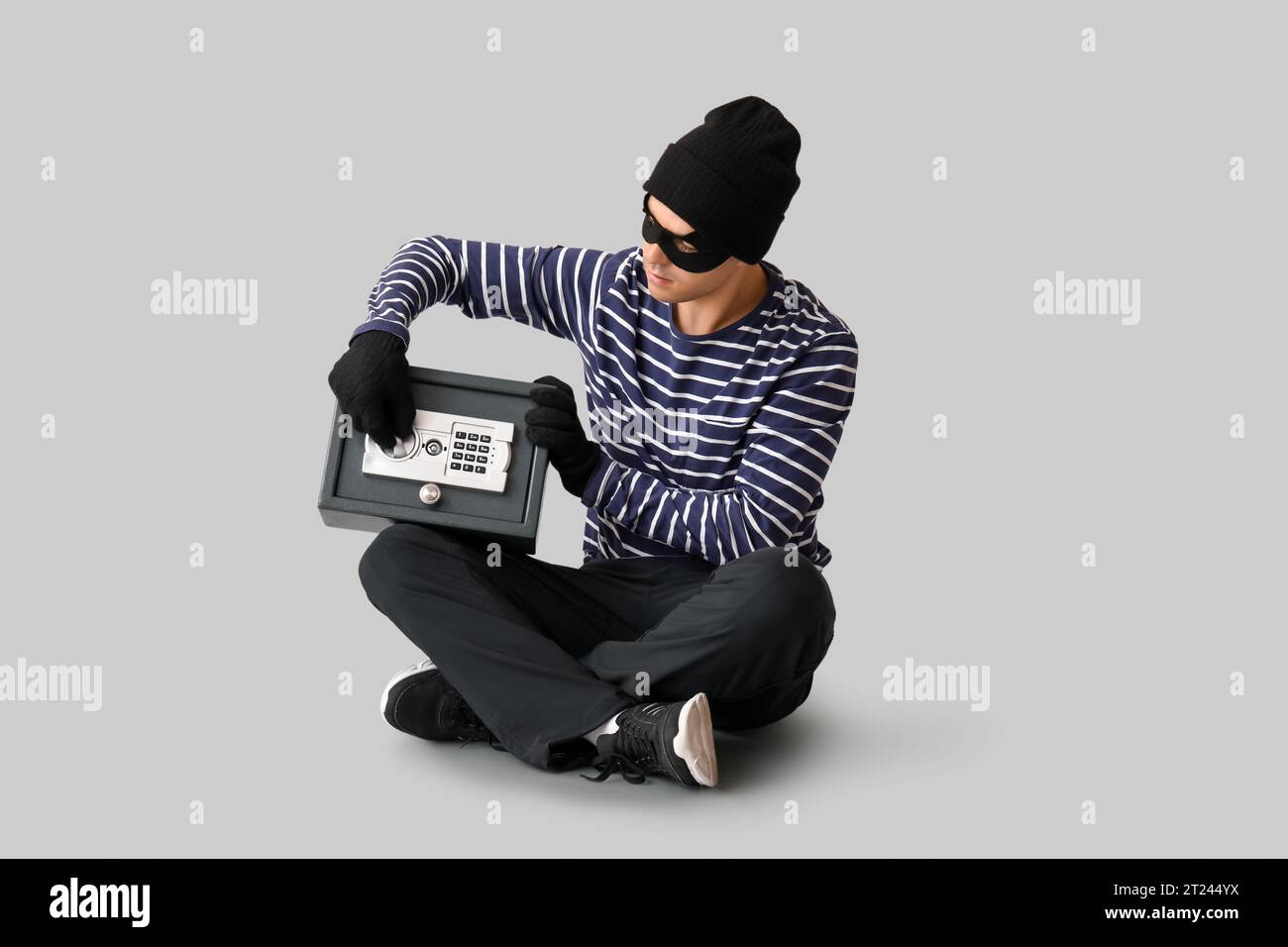 Male thief with safe box on grey background Stock Photo - Alamy