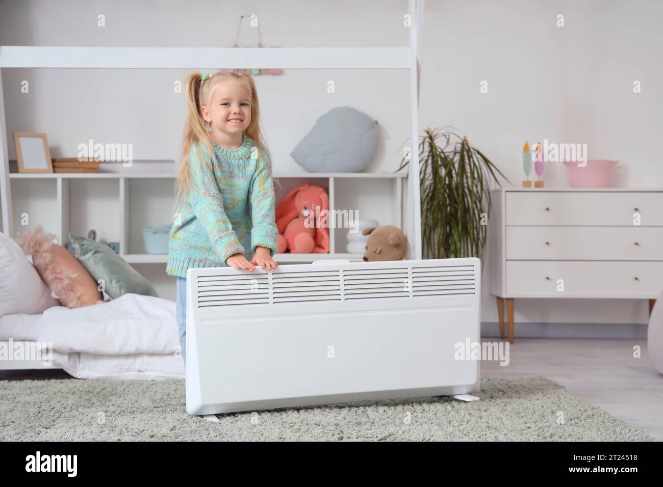 Cute little girl warming near radiator at home Stock Photo - Alamy