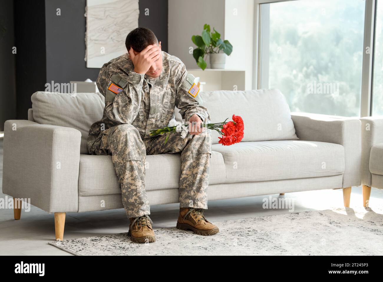 Sad young soldier with flowers at home. Veterans Day celebration Stock ...