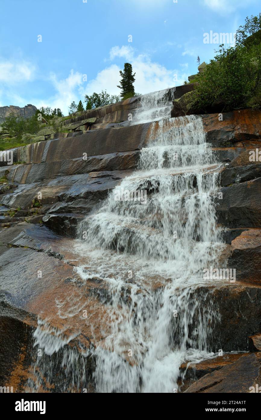A stream of water flows in a stormy cascade from high stone steps of ...