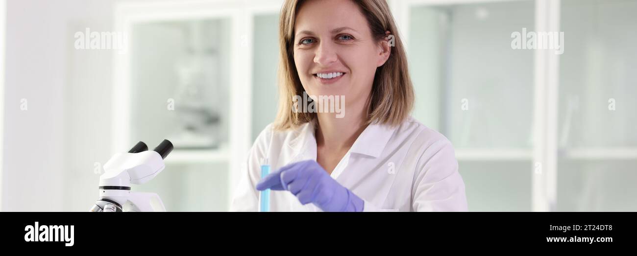 Happy laboratory worker holds tube with blue liquid at table Stock ...