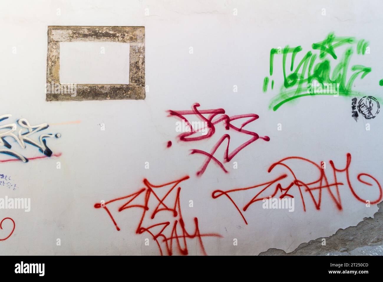 Random graffiti on white wall with old stone window frame, Sopron ...