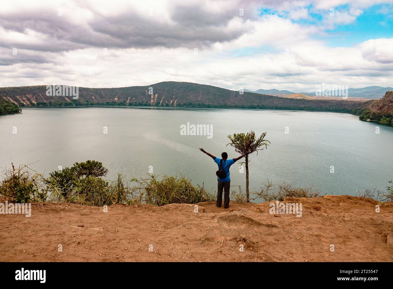 A tourist standing at the shores of Lake Chala with arms outstretched ...