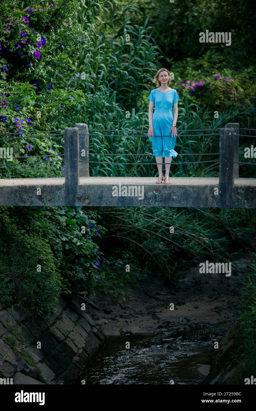 Standing on an ancient suspended bridge is a woman in a blue dress ...