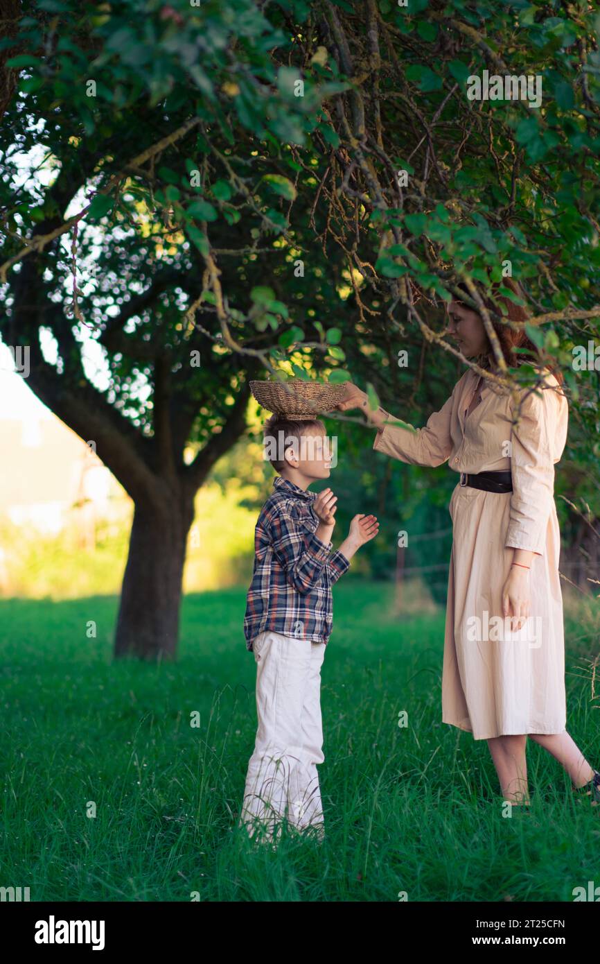 A young beautiful woman with her son in an apple orchard picking apples ...