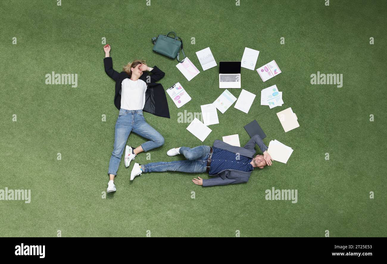 Coworkers lay tired on grass, exhausted employees surrounded with ...