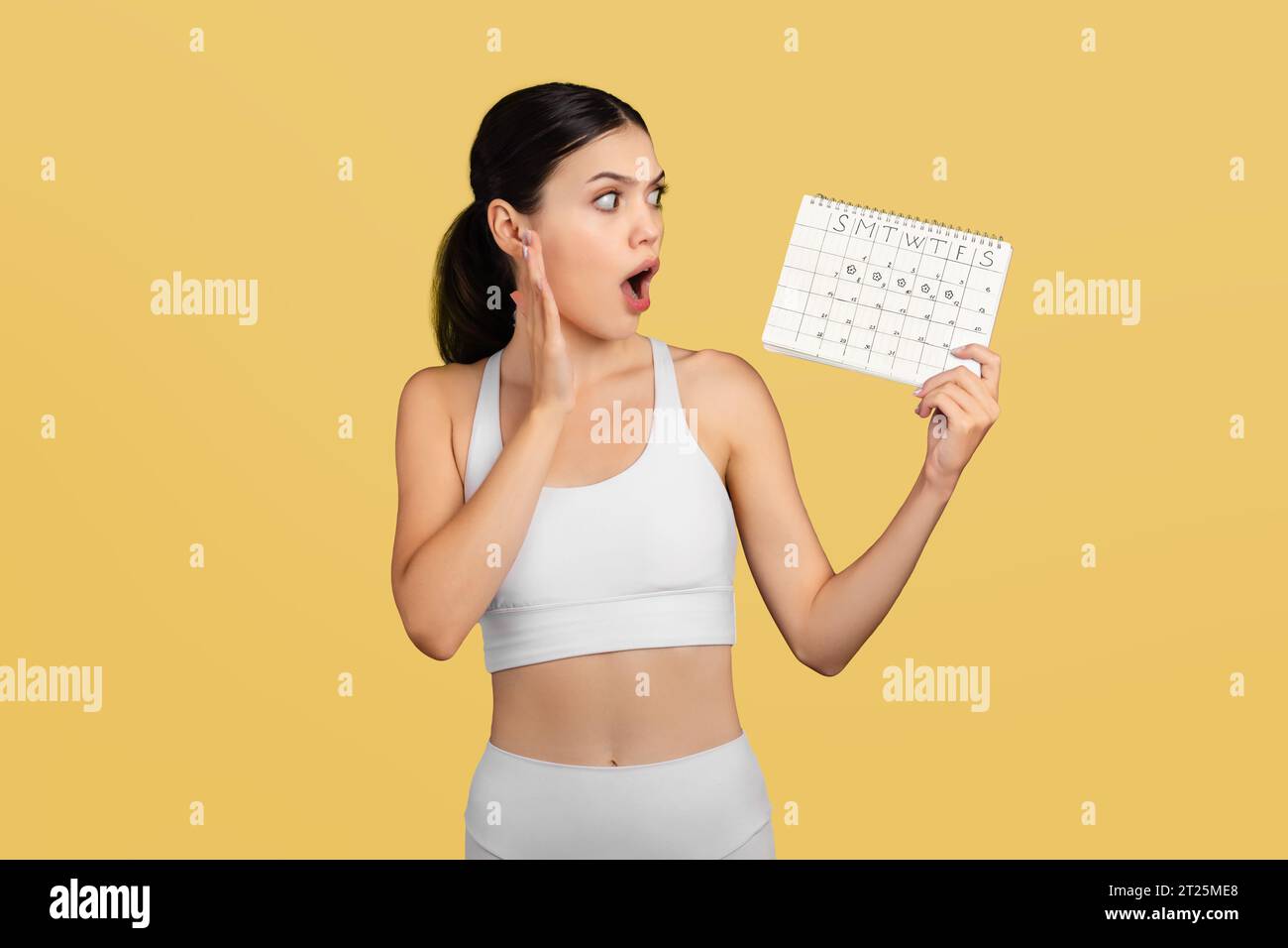 Shocked sporty woman looking at calendar on yellow background Stock ...