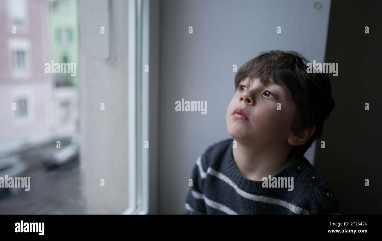 One bored little boy sitting by home window wanting to go out. Child ...