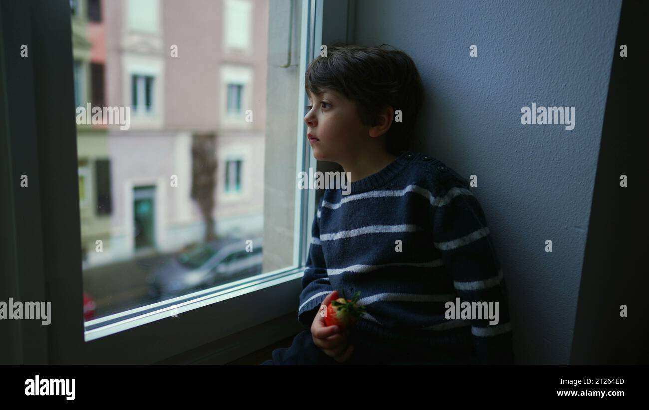 Bored sad emotion of little boy sitting by window staring at view in ...