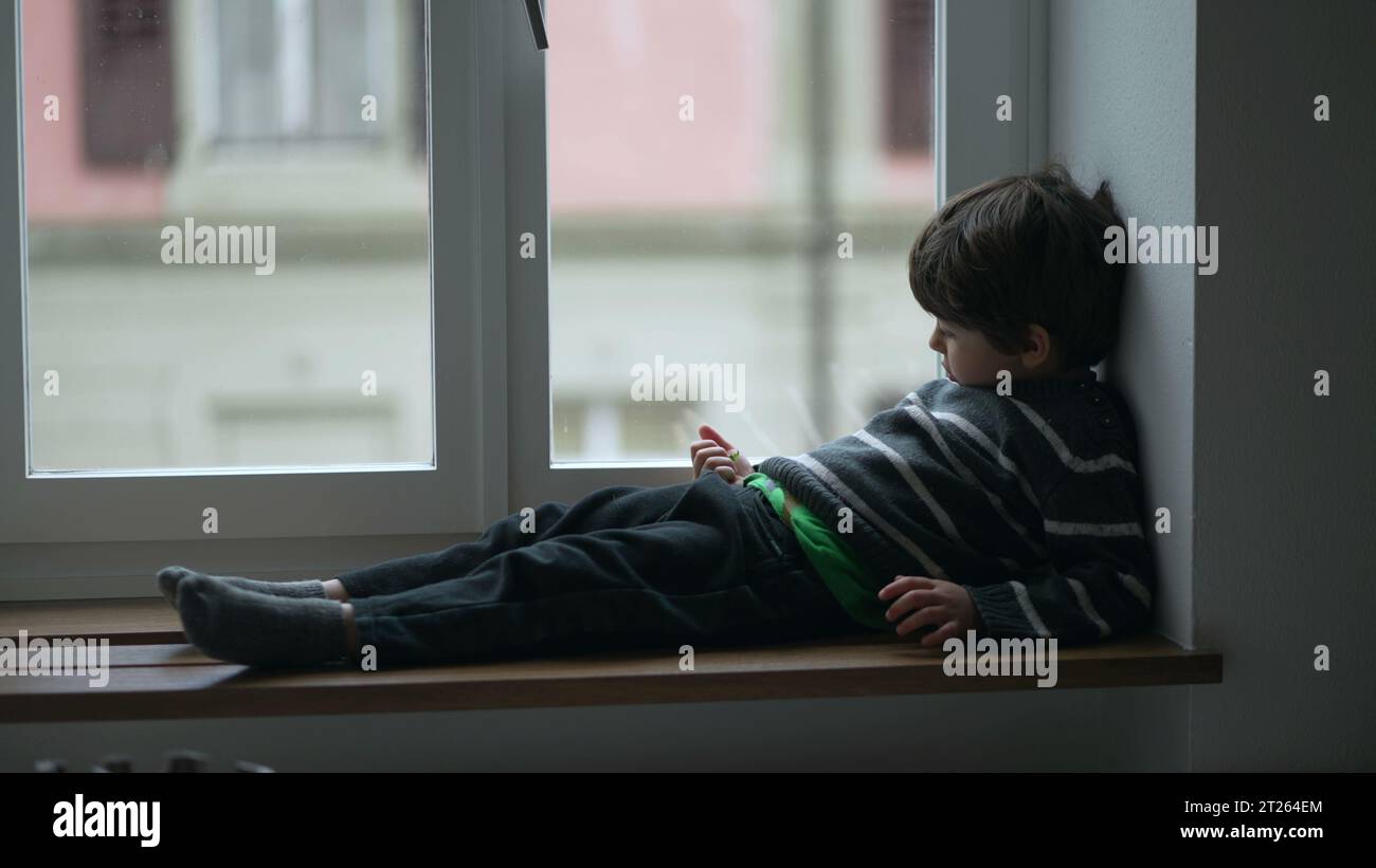 Lazy child sliding down by apartment window, candid bored kid at home ...