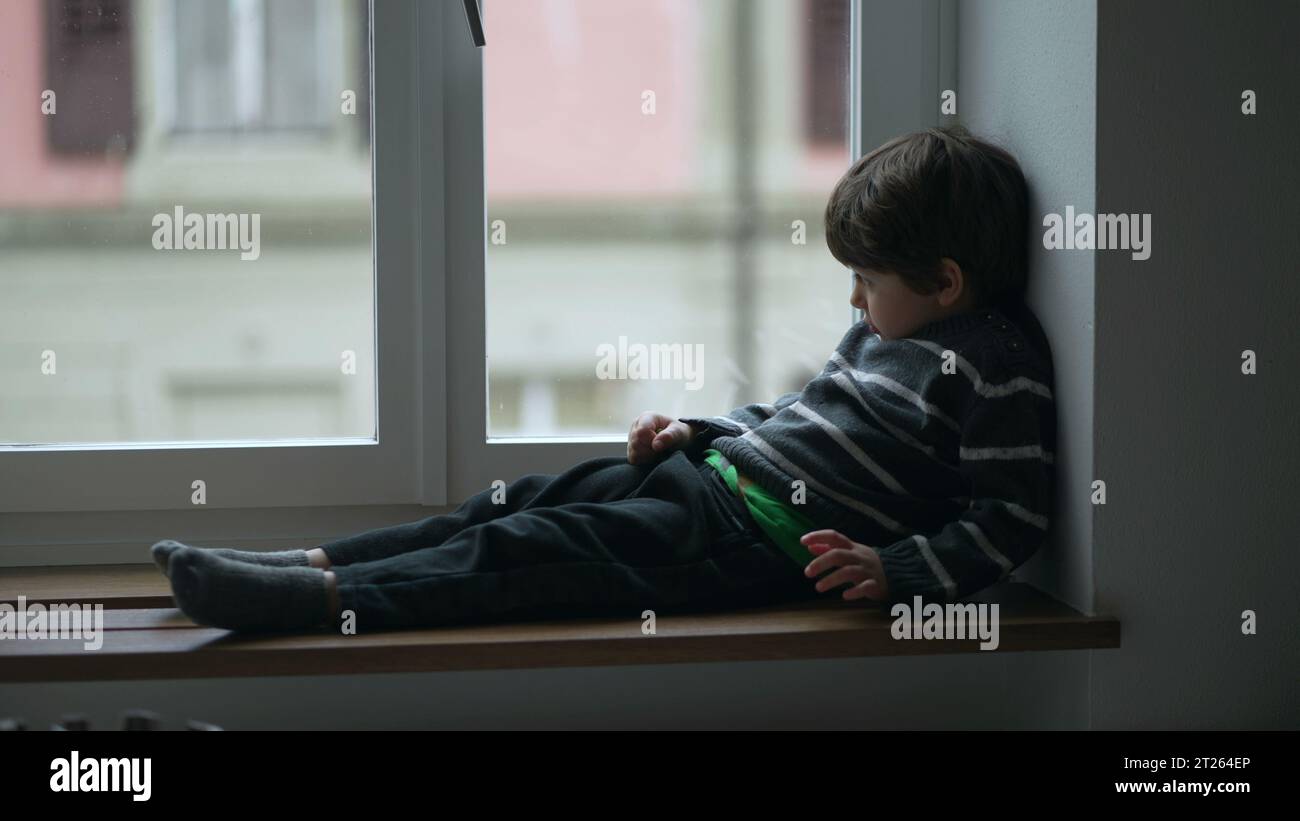 Lazy child sliding down by apartment window, candid bored kid at home ...