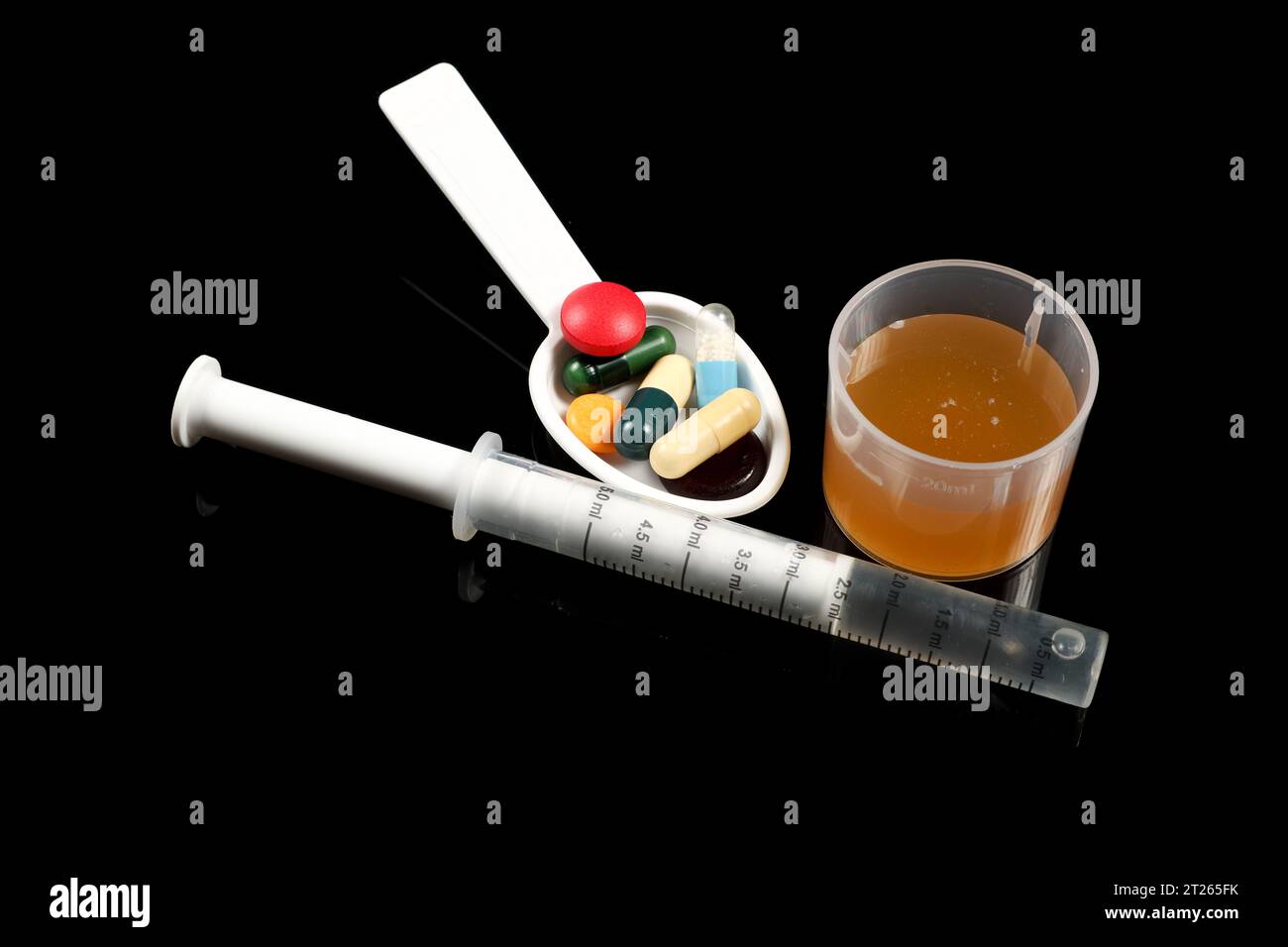 Medicaments in white spoon with syringe and syrup isolated on black ...