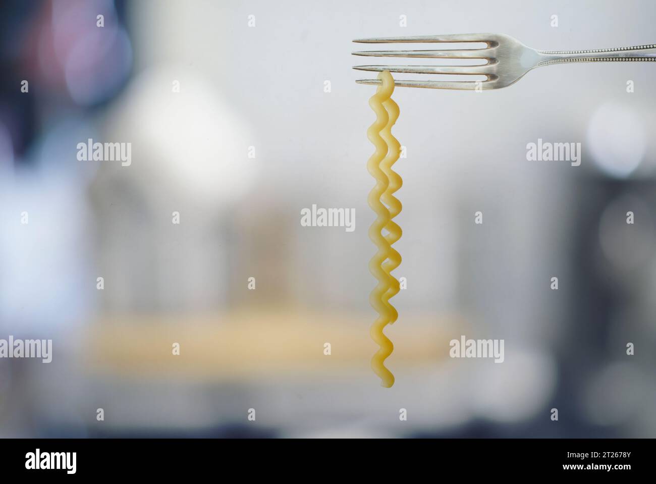 italian pasta hanging from a silver fork, isolated on blurred kitchen ...