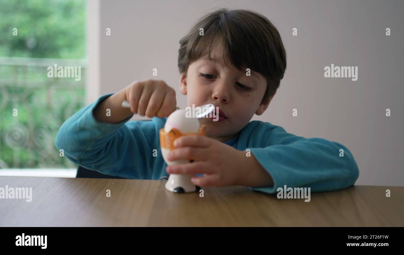 Child breaking soft boiled egg with spoon, preparing to eat oeuf a la ...