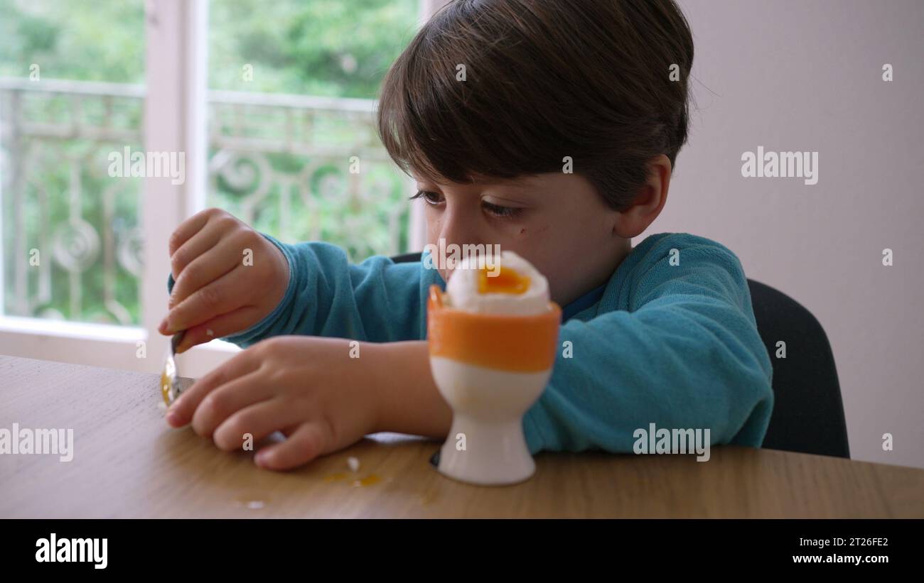Child eating soft boiled egg with spoon, small boy cracking the top of ...