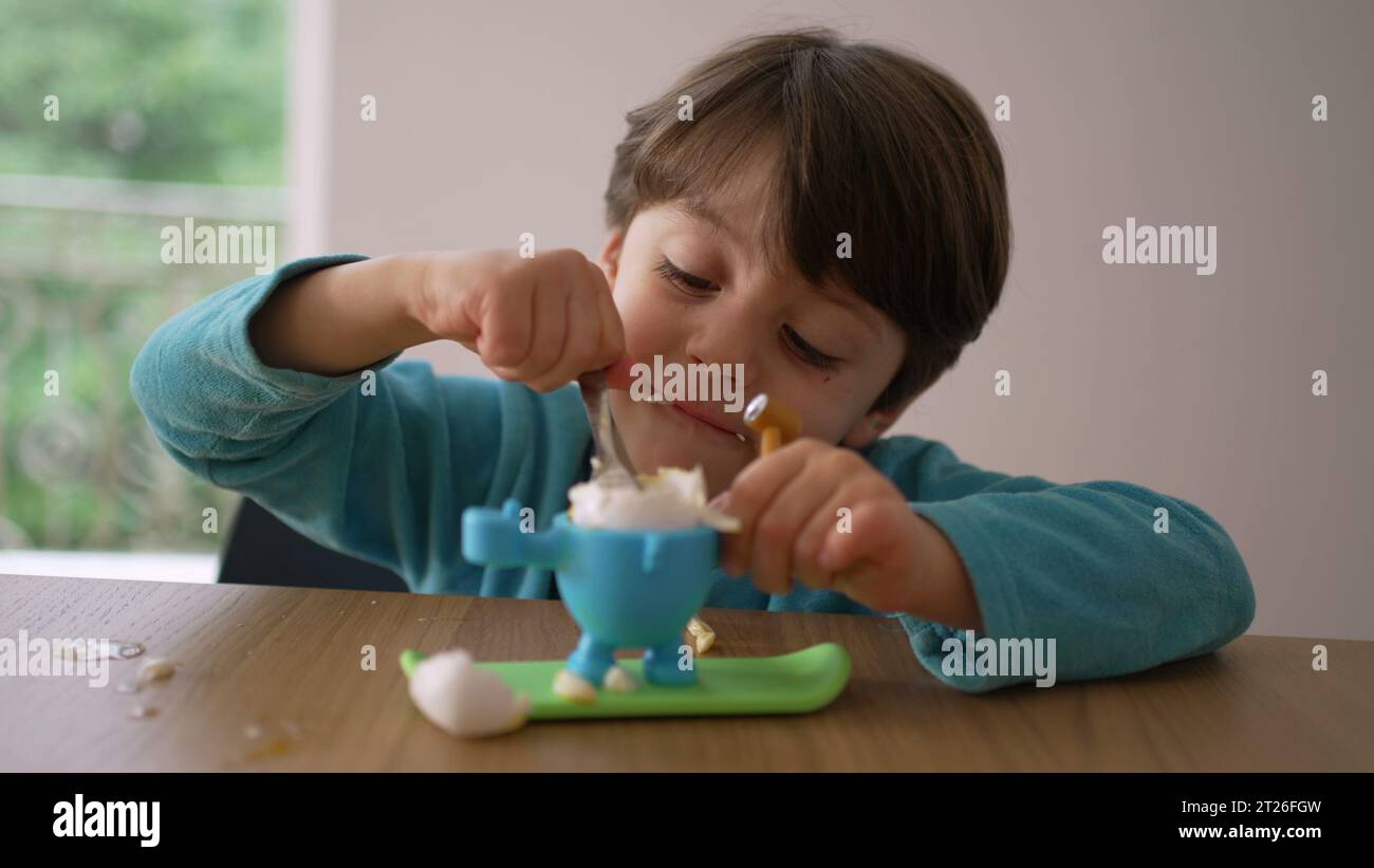 Concentrated child eating soft boiled egg in the evening, dining ...
