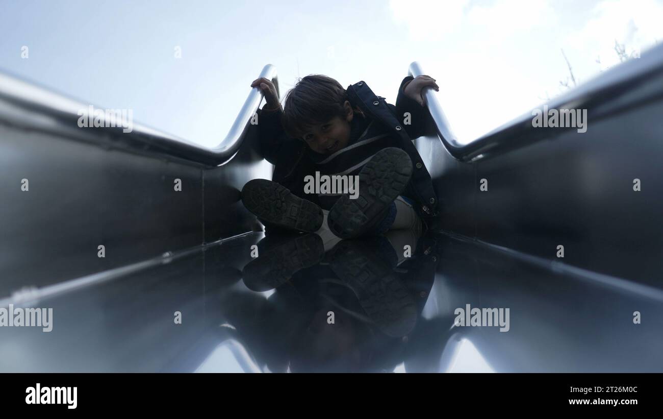 Joyful child sliding down slider at playground park during fall season ...
