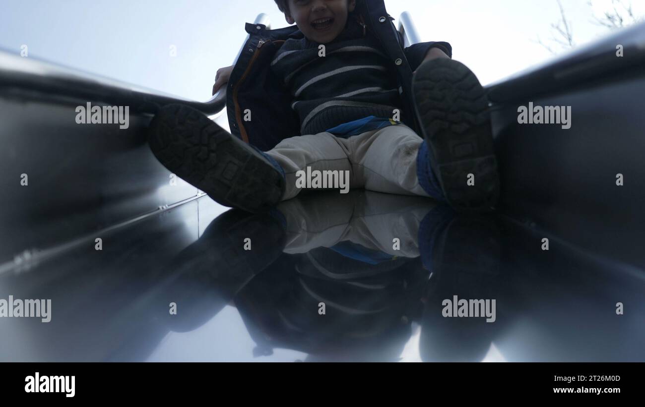Joyful child sliding down slider at playground park during fall season ...