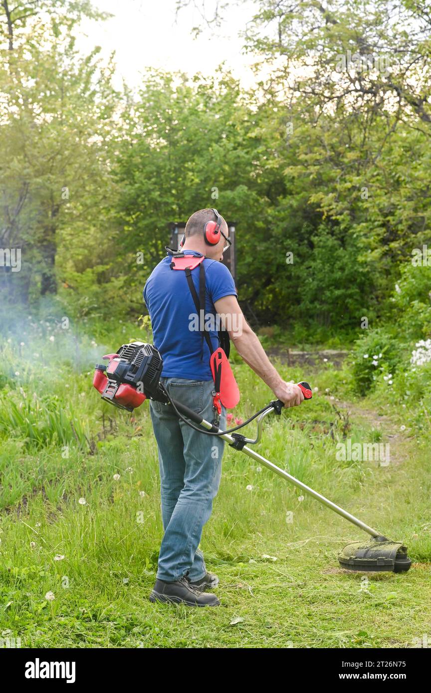 A gardener mows the green grass of the lawn in the backyard with a ...