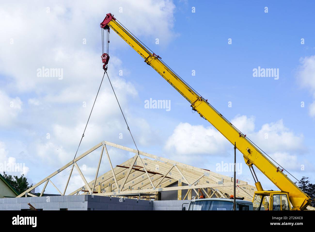 Mobile crane with yellow telescopic boom has lifted the wooden roof ...