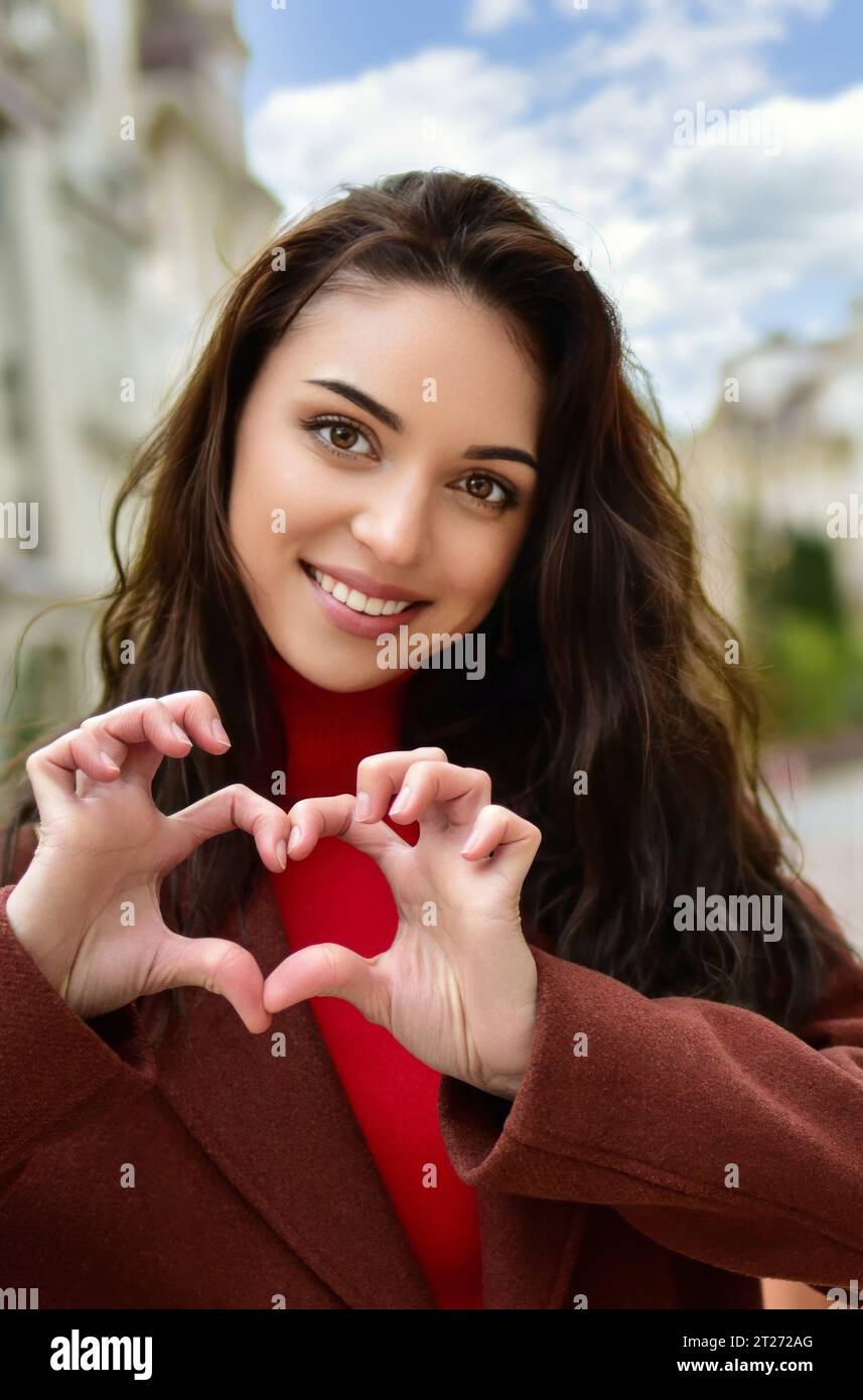 Fashionable smiling woman shows the sign of love with her fingers ...