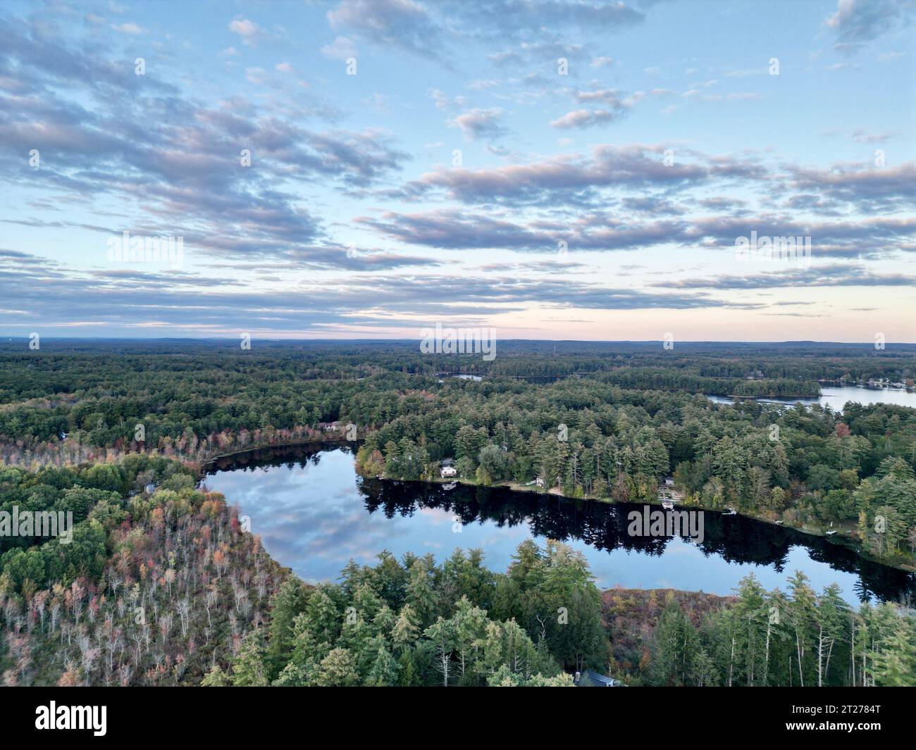An idyllic lake and wooded landscape under a cloudy sky with a glimmer ...