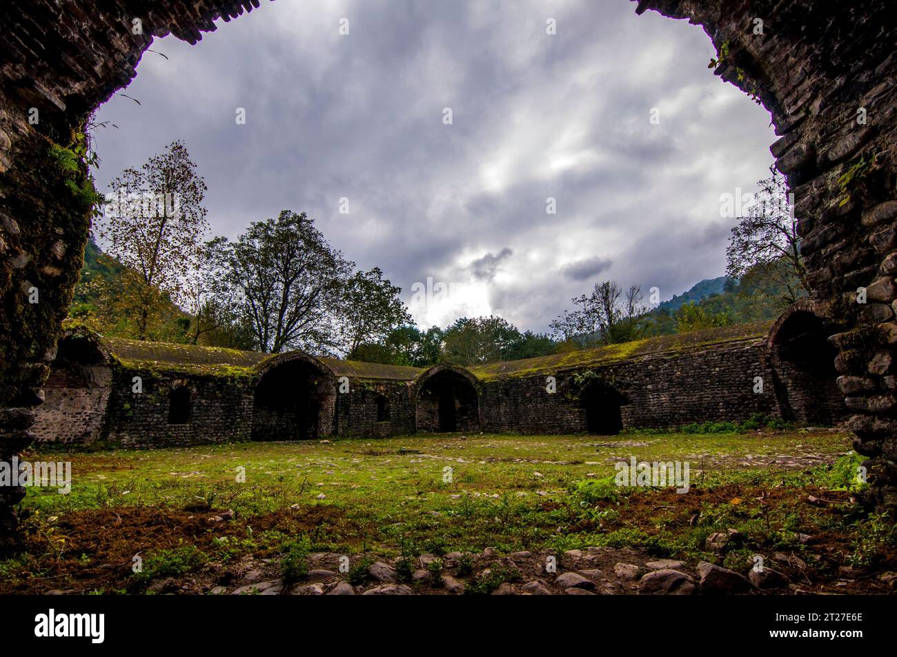 An abandoned stone tunnel leads the way down a path of overgrown grass ...