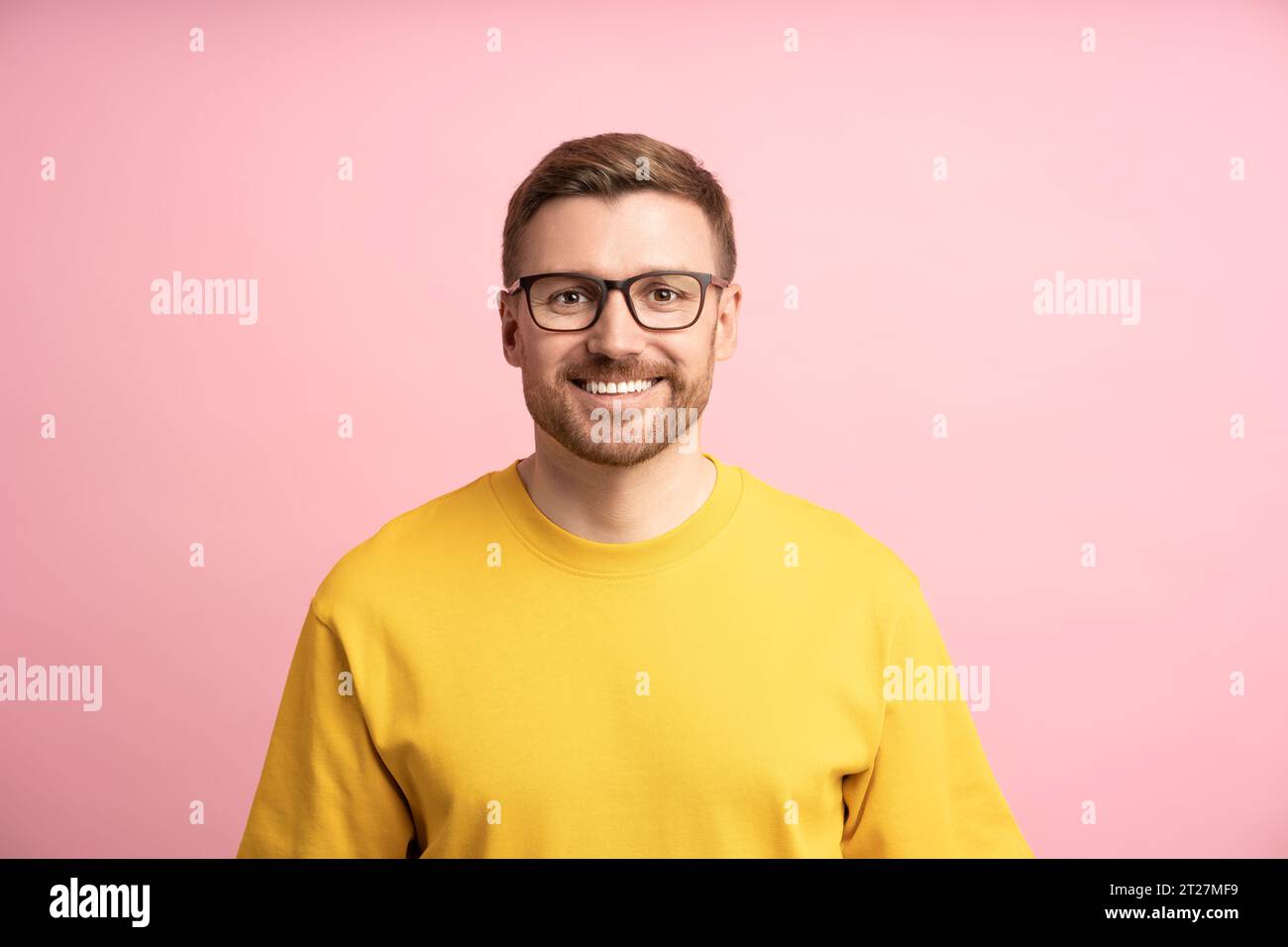 Pleased man smiling, portrait on pink studio wall. Educated guy smart ...