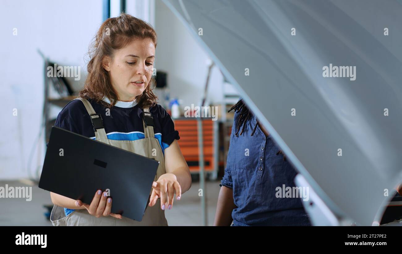 Mechanic in garage talking with client and using laptop to order new ...