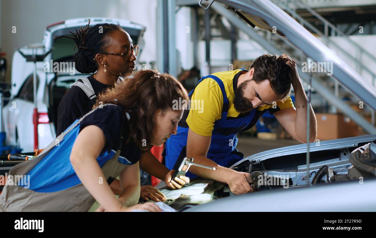 Team of technicians in car service using inspection lamp to fix damaged ...