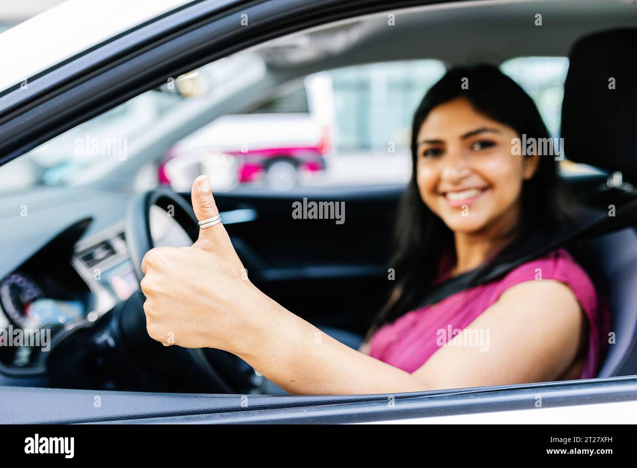Happy young adult indian woman doing ok sign gesture sitting on her car ...