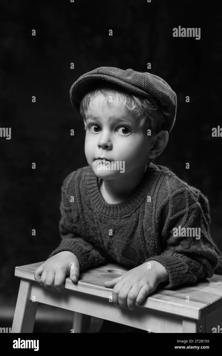 A little boy in a sweater and a retro-style cap on a dark background ...