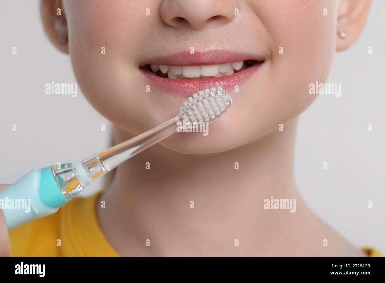Girl brushing her teeth with electric toothbrush on light grey ...
