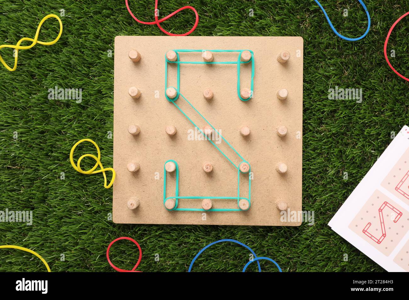 Wooden geoboard with letter S made of rubber bands on artificial grass ...