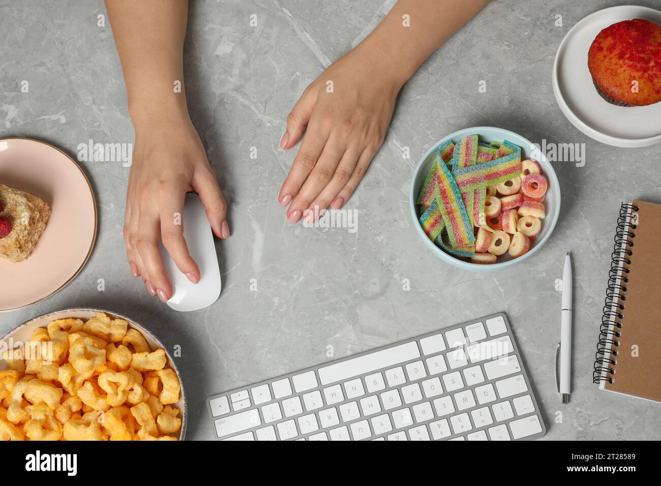 Bad eating habits. Woman working on computer at grey marble table with ...