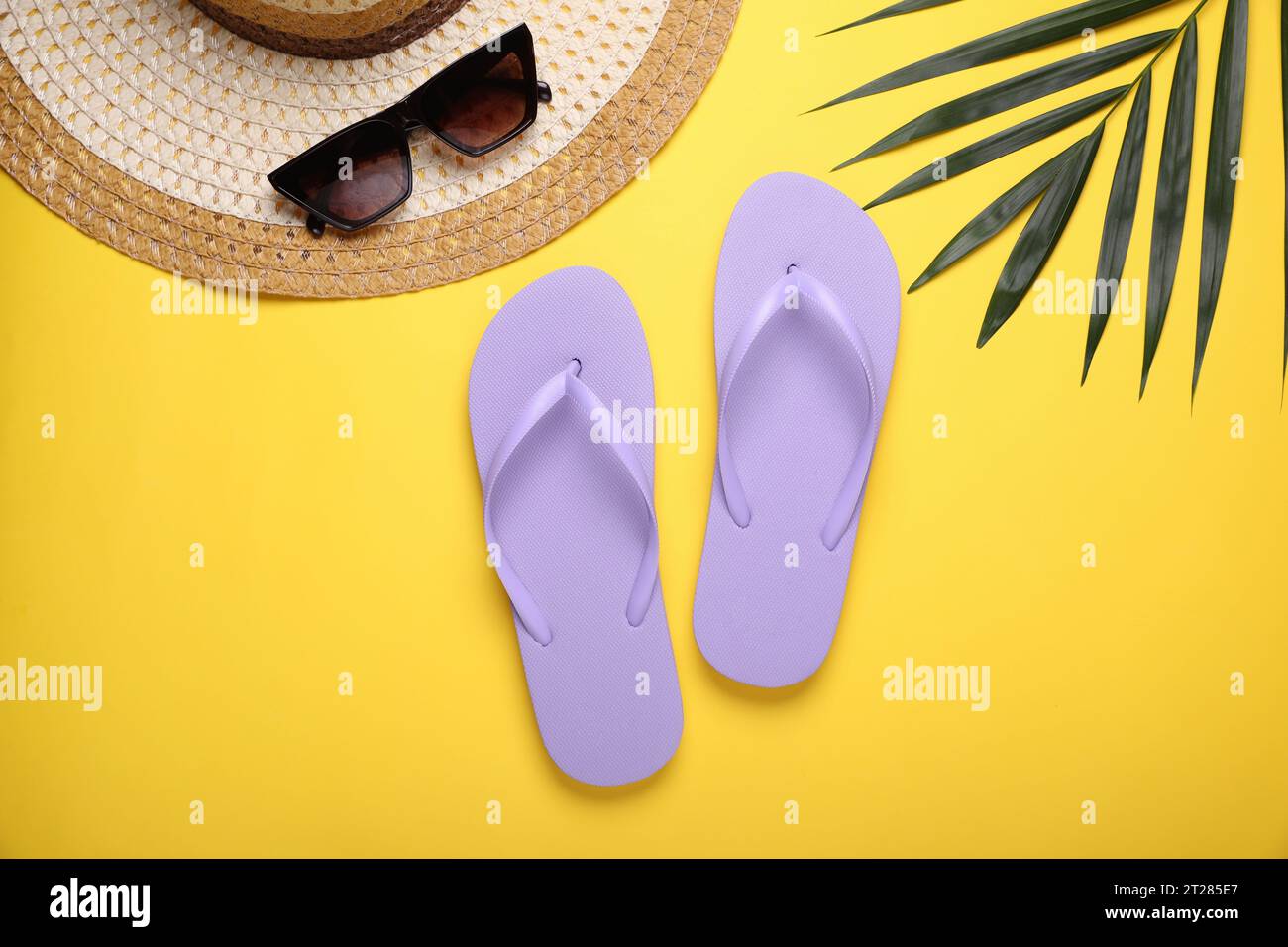 Stylish flip flops, sunglasses, hat and palm leaf on yellow background ...