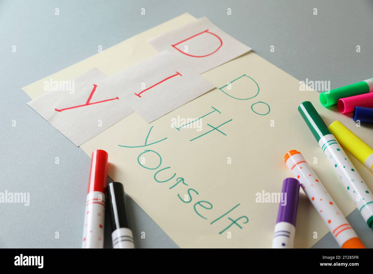 Sheet with written phrase Do It Yourself and colorful markers on grey ...