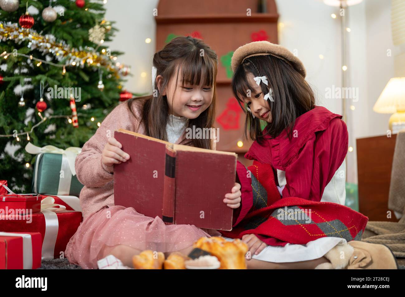 Two joyful and cute young Asian girls are enjoying reading a Christmas ...