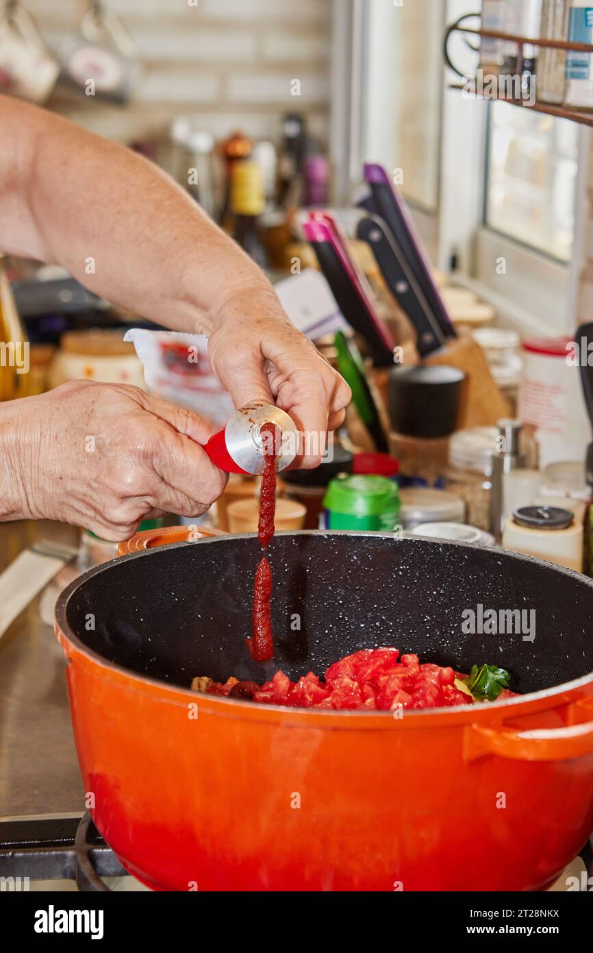 Chef puts tomato paste from tube into pan with meat on gas stove Stock ...