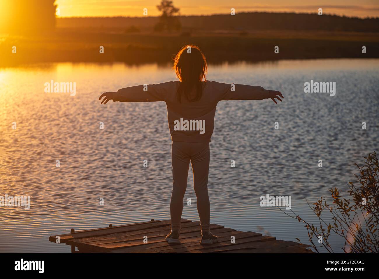 A cute girl standing on the pier, bridge by the river at sunset ...
