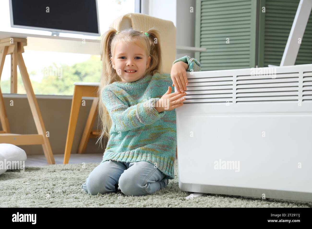 Cute little girl warming near radiator at home Stock Photo - Alamy