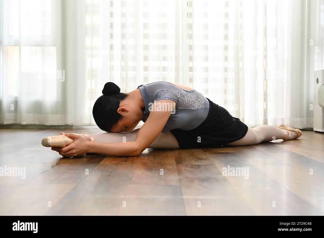 Beautiful ballerina doing splits on the wooden floor stretching legs ...