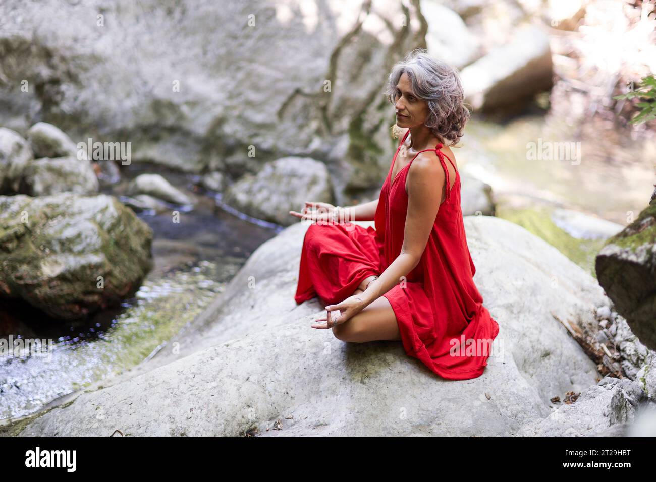 Religious woman doing yoga in long red dress, in wild nature, near to ...