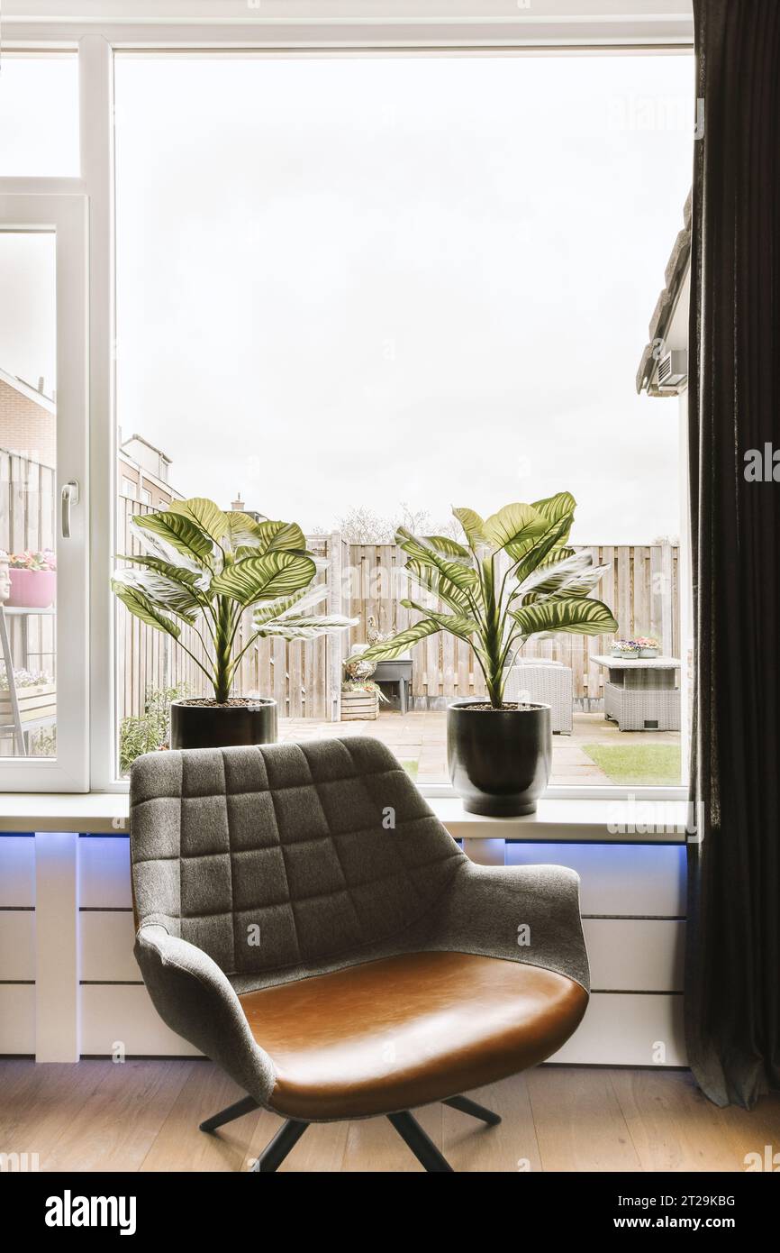 Empty lounge chair next to bright window with potted plants on sill at ...