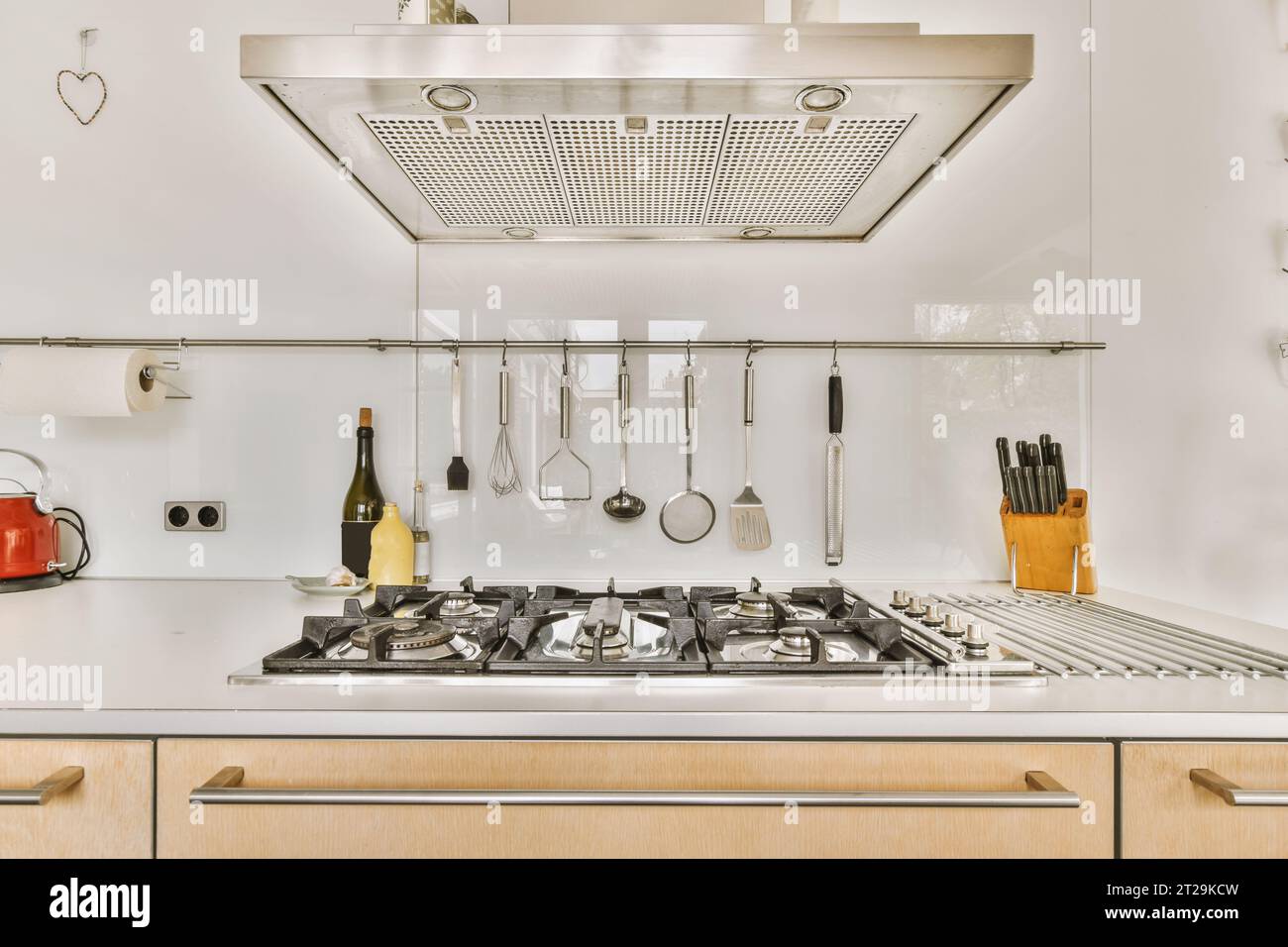 Steel hood over stove with utensils hanging in front of white tiled ...