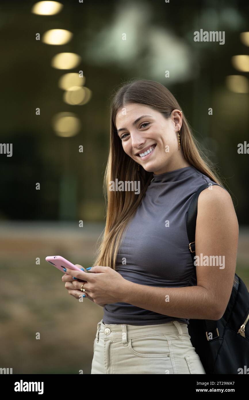 Beautiful cheerful young lady looking at camera texting and standing ...