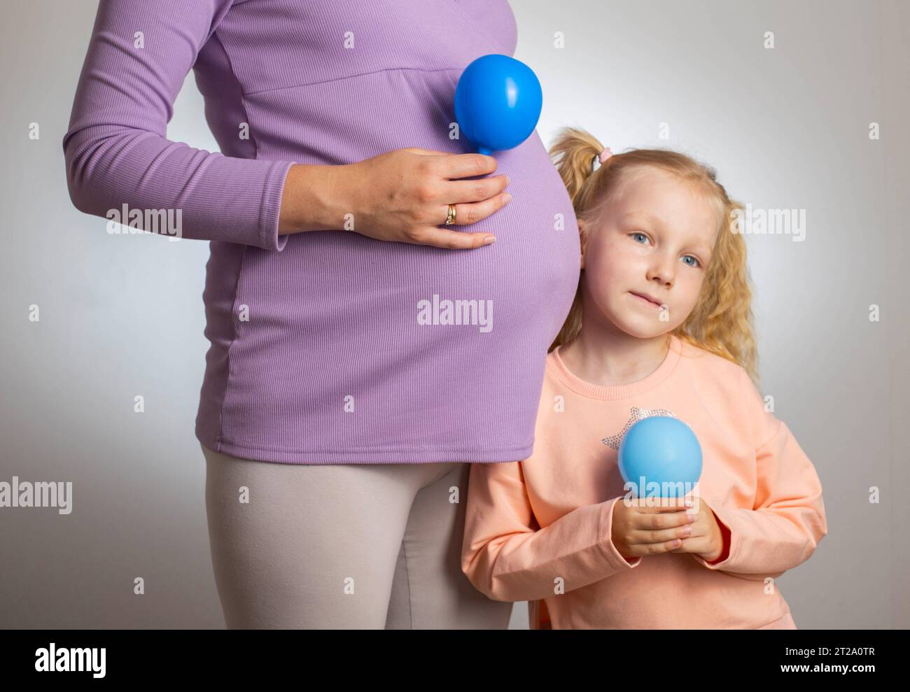 A pregnant mother and daughter are holding blue balloons in their hands ...