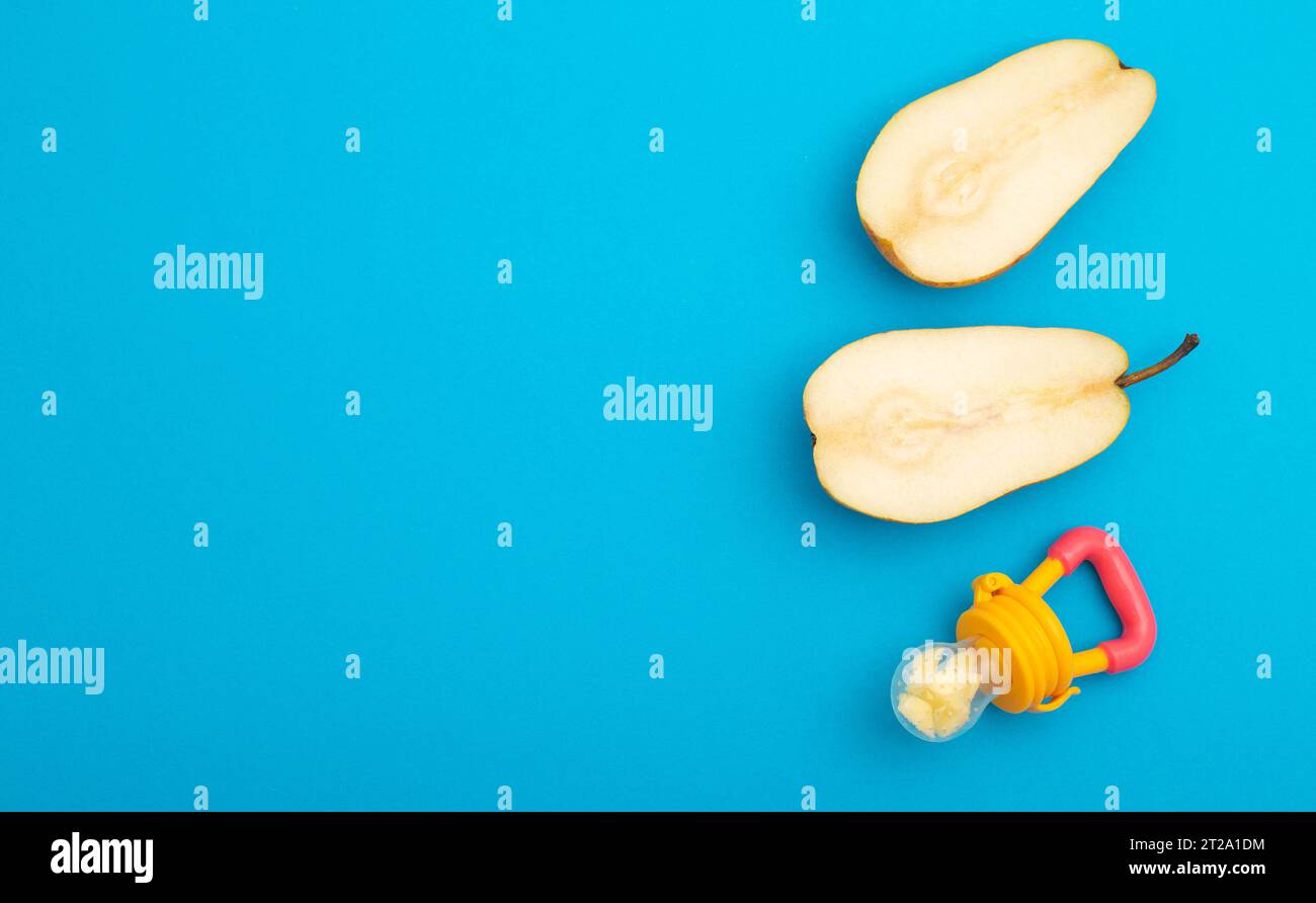 A pear cut in half on a blue background and a baby nibbler for feeding ...